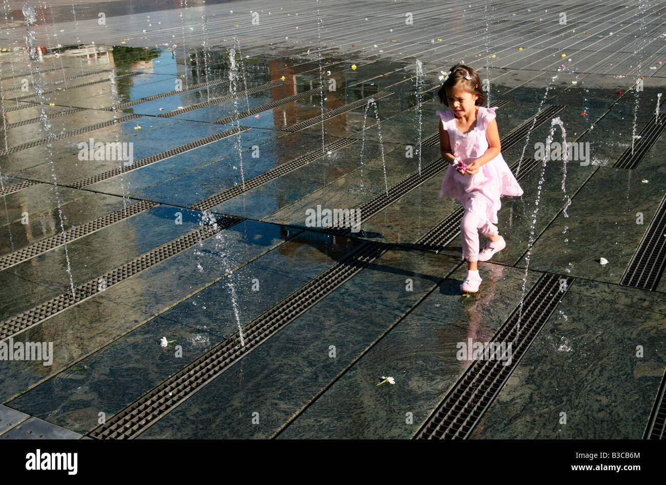 Young girl child kid running between many water fountain stream nozzle ...