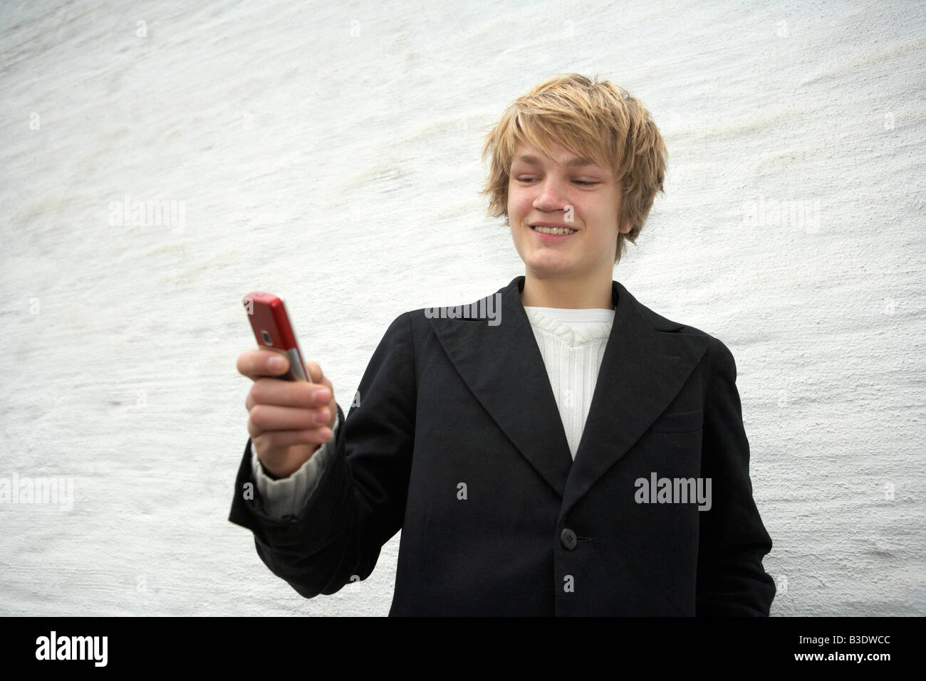 Smiling teenage boy looking at mobile phone by building wall Stock ...