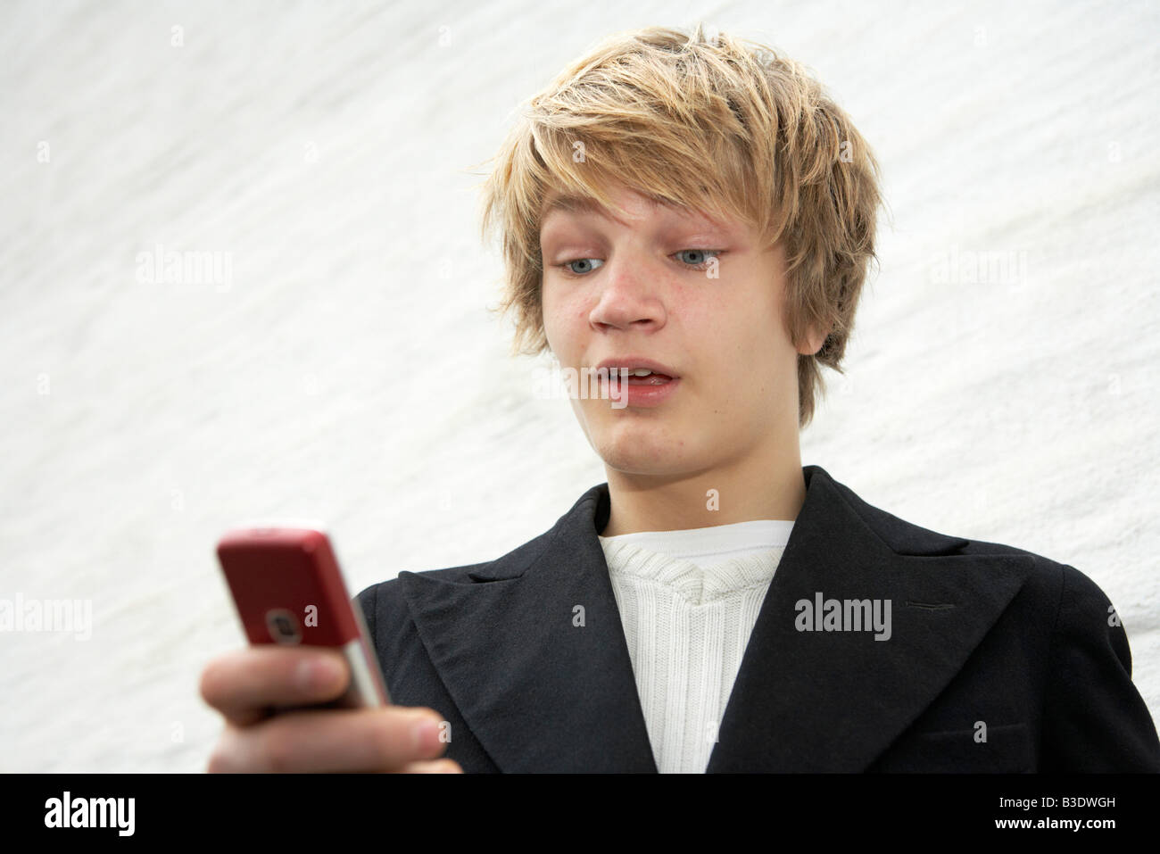 Teenage boy looking at mobile phone by building wall surprised ...
