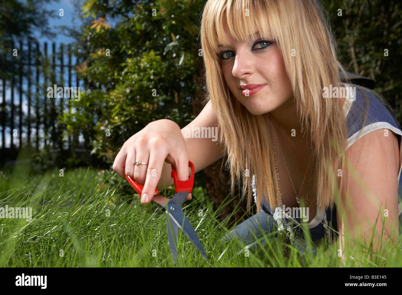 young blonde haired woman late teens early twenties cutting grass in a ...