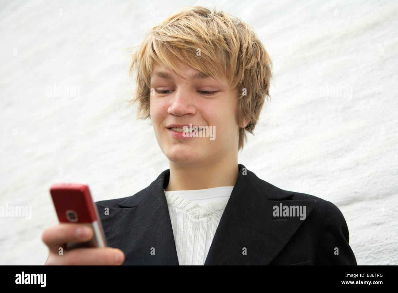 Teenage boy looking at mobile phone by building wall smiling Stock ...