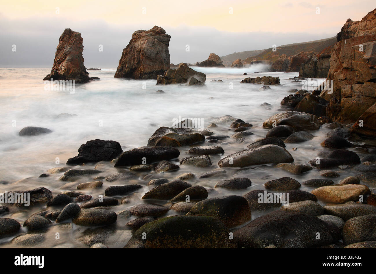 A rocky beach with moving waves with two pinnacles sticking out of the ...
