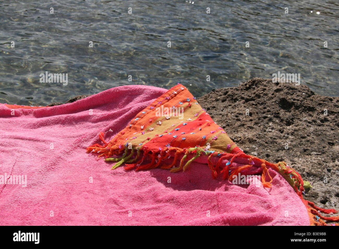 one red towel in sun on rocks beach by sea Stock Photo - Alamy