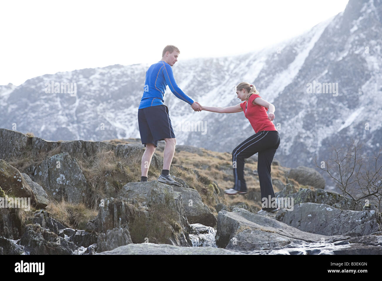 A man helping a woman over rocks Stock Photo - Alamy