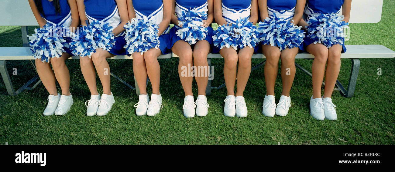 Group of cheerleaders sitting in row on bench, low section Stock Photo ...