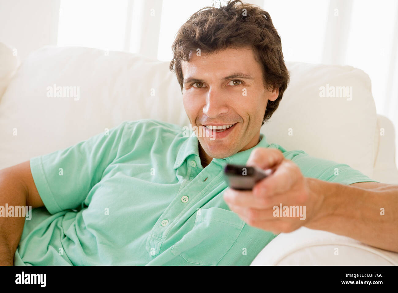 Man in living room holding remote control smiling Stock Photo - Alamy