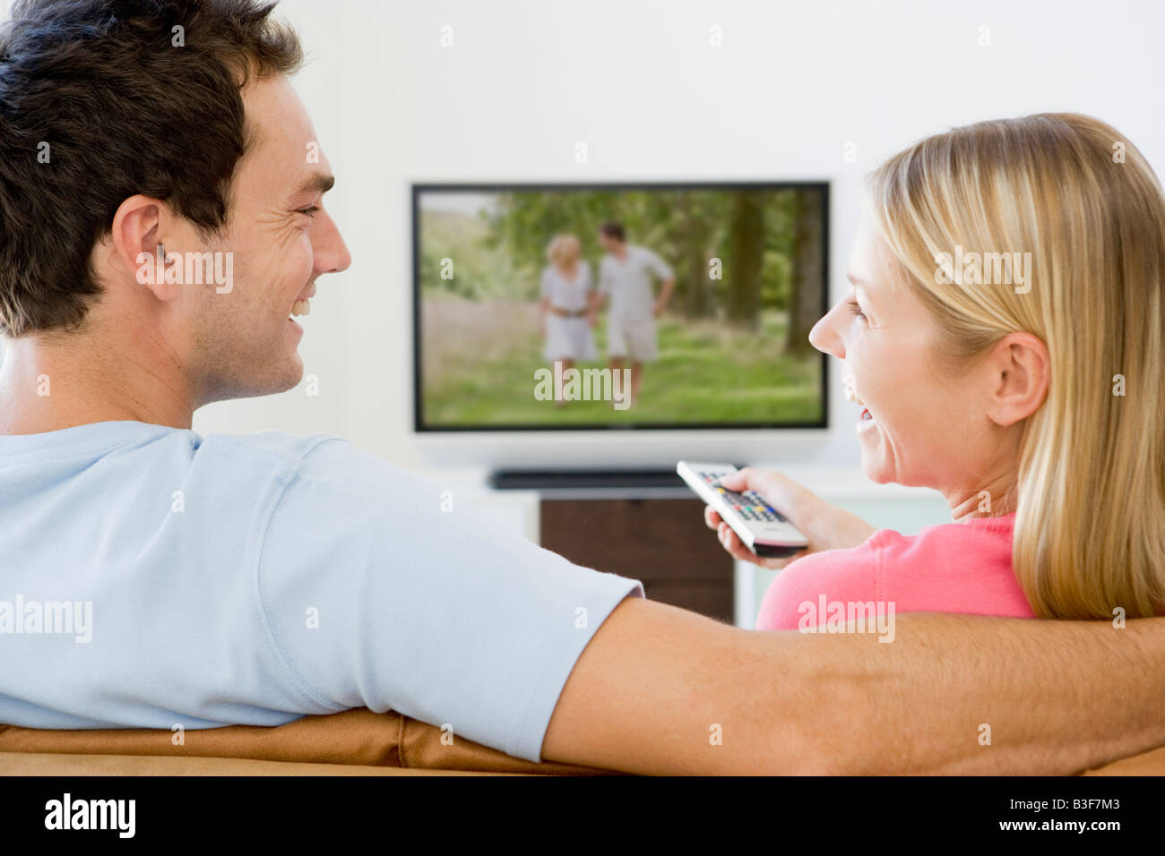 Couple in living room watching television smiling Stock Photo - Alamy