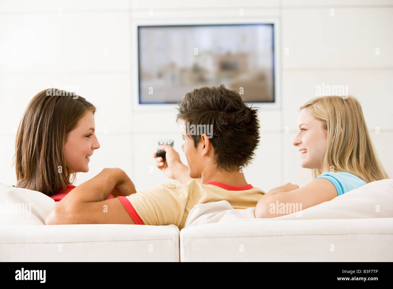 Three friends in living room watching television smiling Stock Photo ...