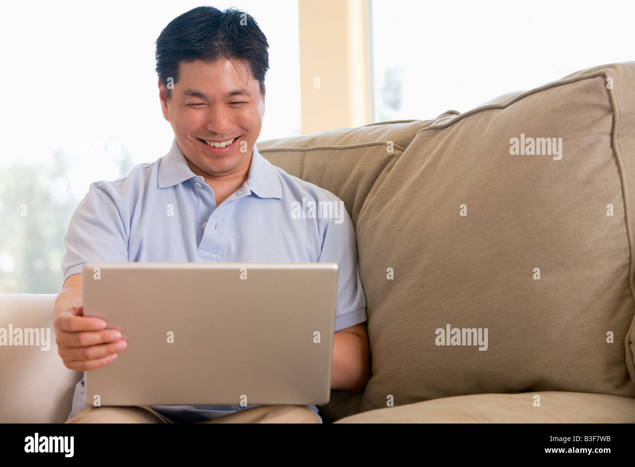 Man in living room using laptop and smiling Stock Photo - Alamy
