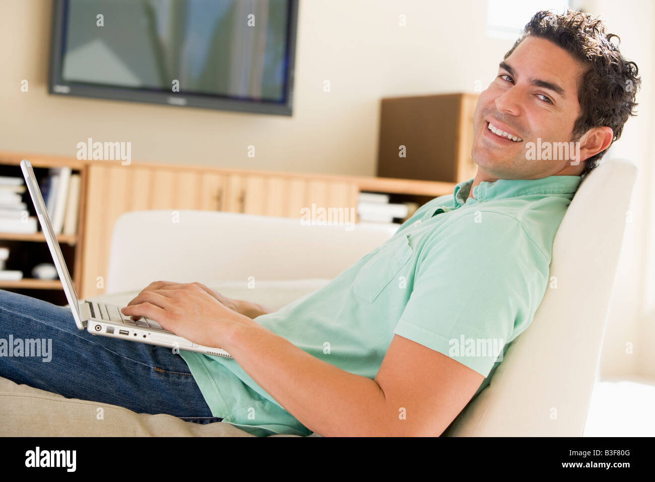 Man in living room using laptop smiling Stock Photo - Alamy