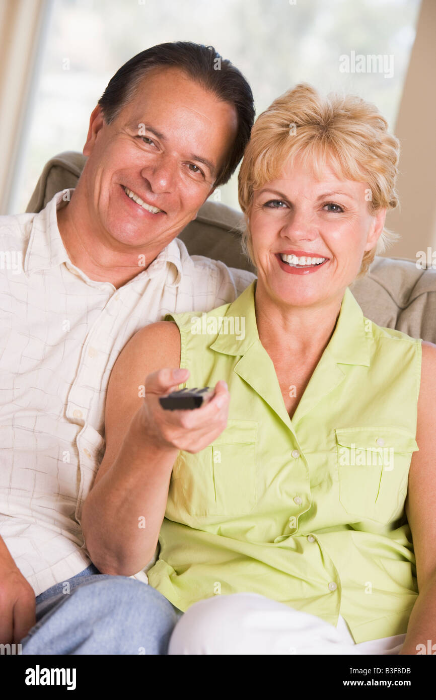 Couple in living room using remote control smiling Stock Photo - Alamy