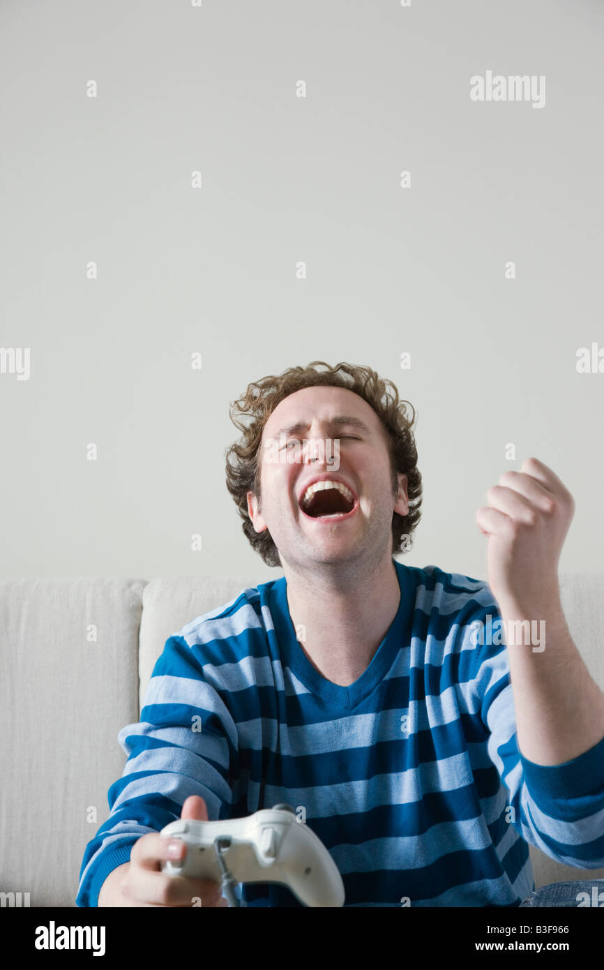 Man holding computer game controls laughing on sofa Stock Photo - Alamy