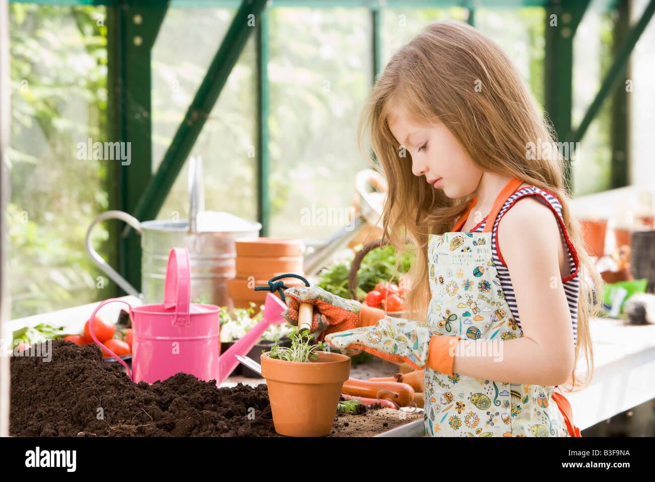 Young girl in greenhouse putting plant in pot Stock Photo - Alamy