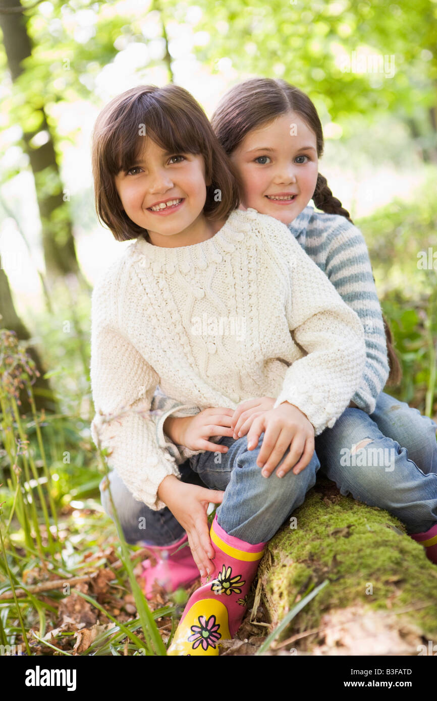Two sisters outdoors in woods sitting on log smiling Stock Photo - Alamy