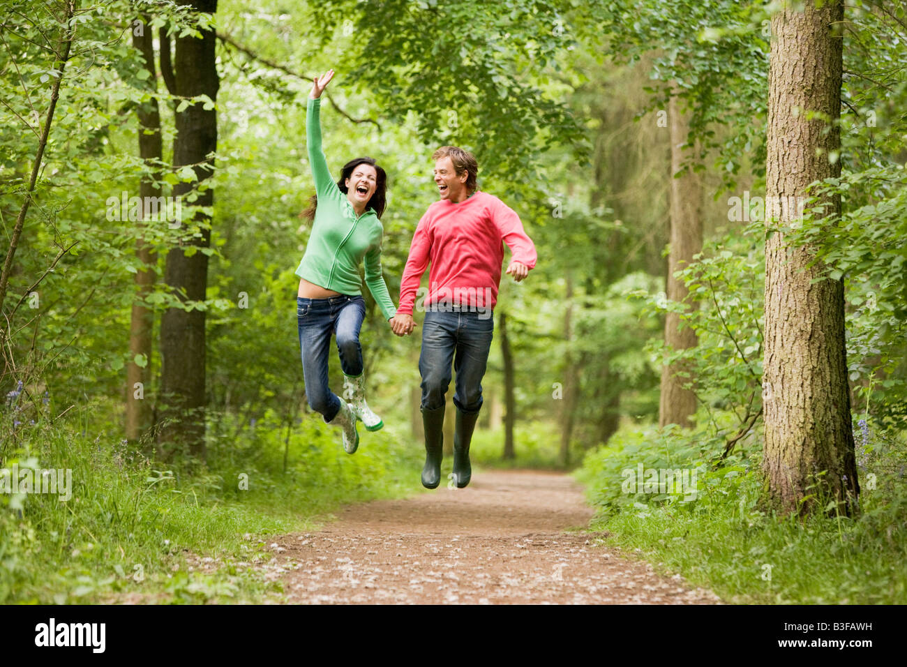 Couple jumping on path holding hands and smiling Stock Photo - Alamy