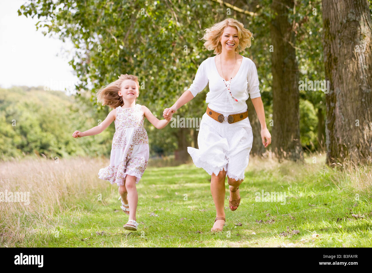 Mother and daughter walking on path holding hands smiling Stock Photo ...