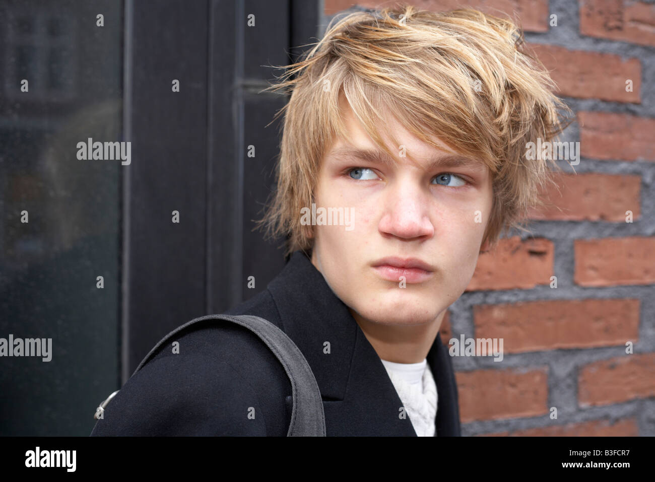 Teenage boy looking over shoulder by building wall Stock Photo - Alamy