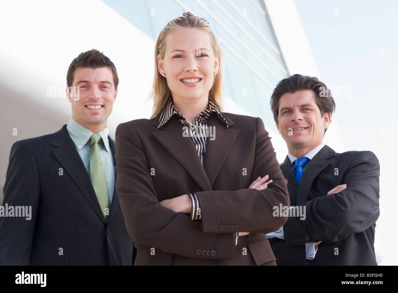 Three businesspeople standing outdoors by building smiling Stock Photo ...