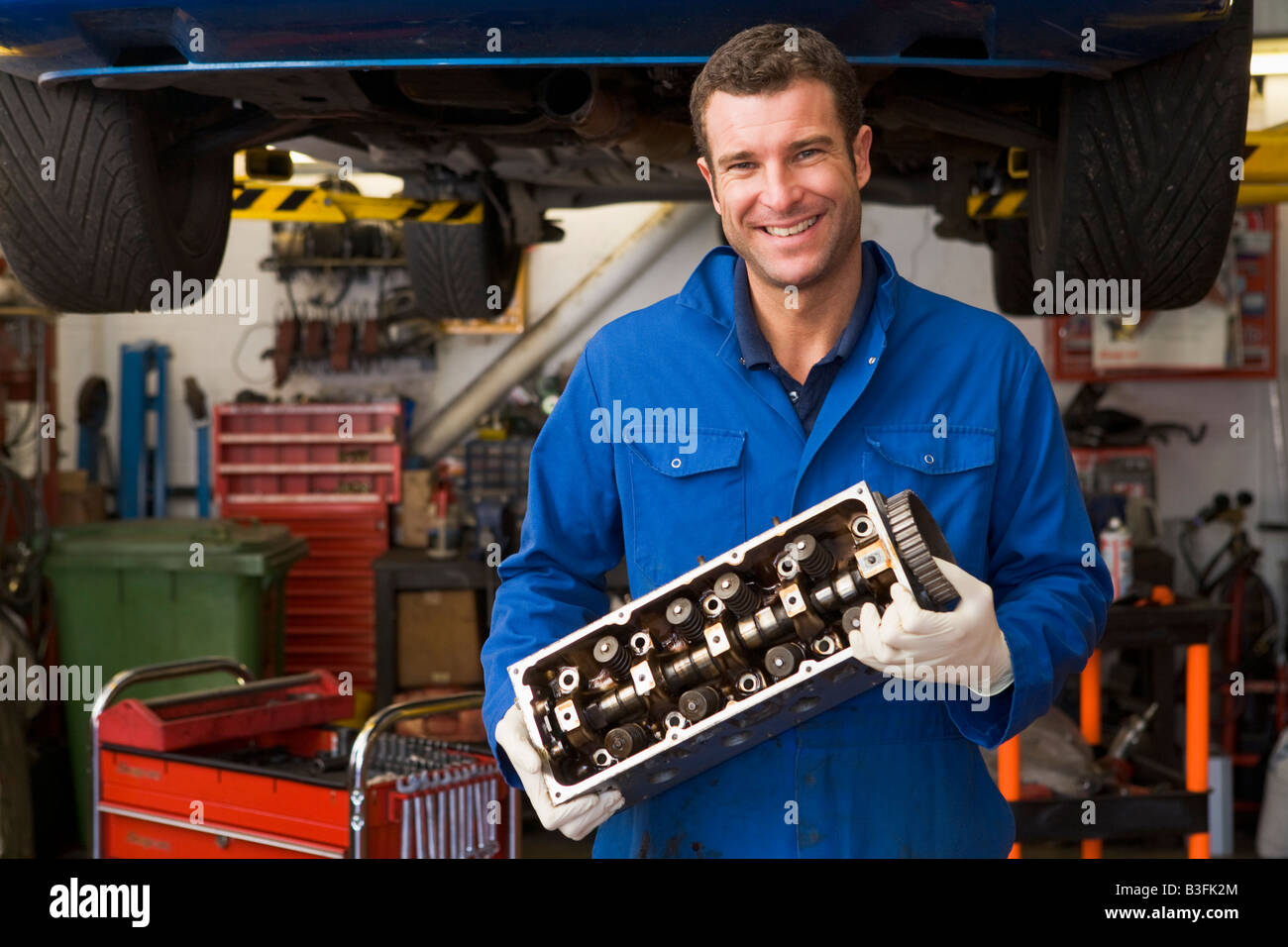 Mechanic holding car part smiling Stock Photo - Alamy