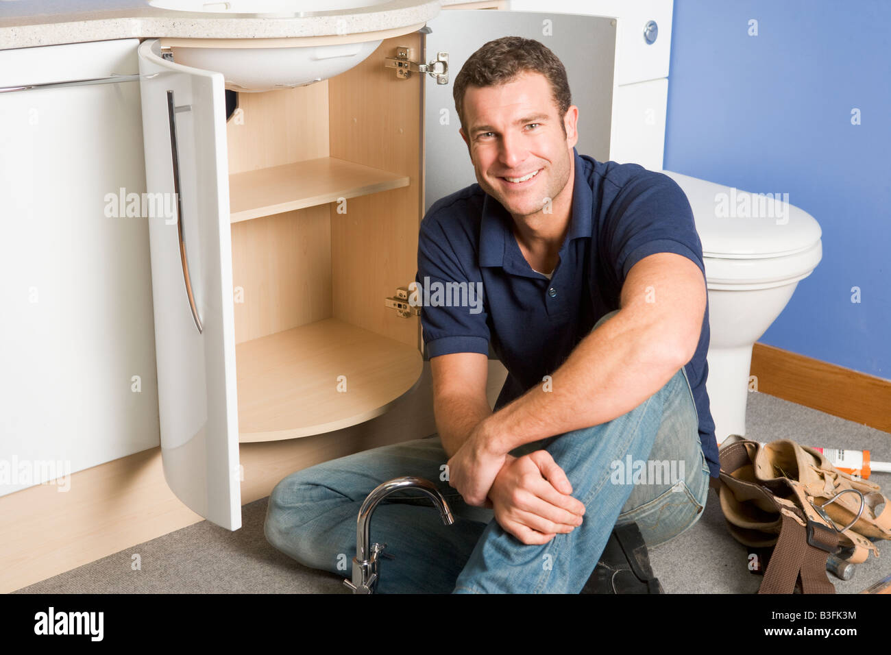 Plumber working on sink smiling Stock Photo - Alamy