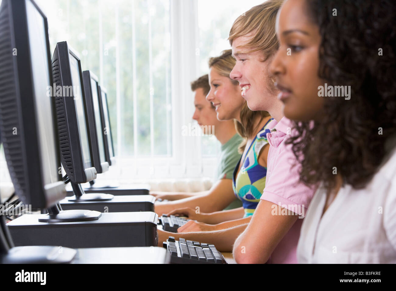 Four people sitting at computer terminals (selective focus/high key ...