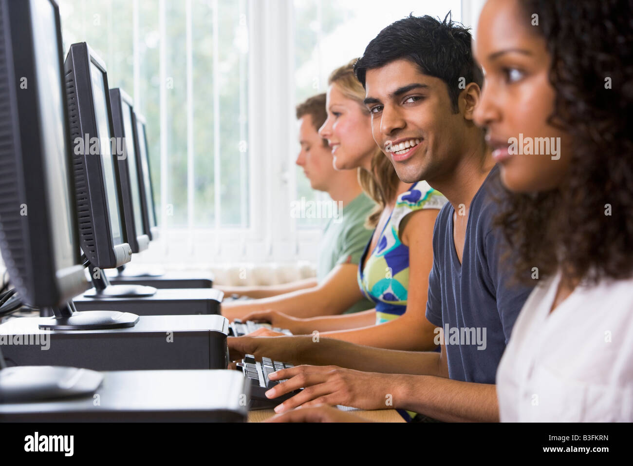 Four people sitting at computer terminals (selective focus/high key ...