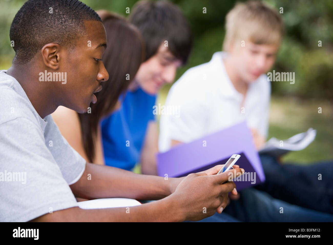 Four students outdoors studying with one checking cellular phone (depth ...