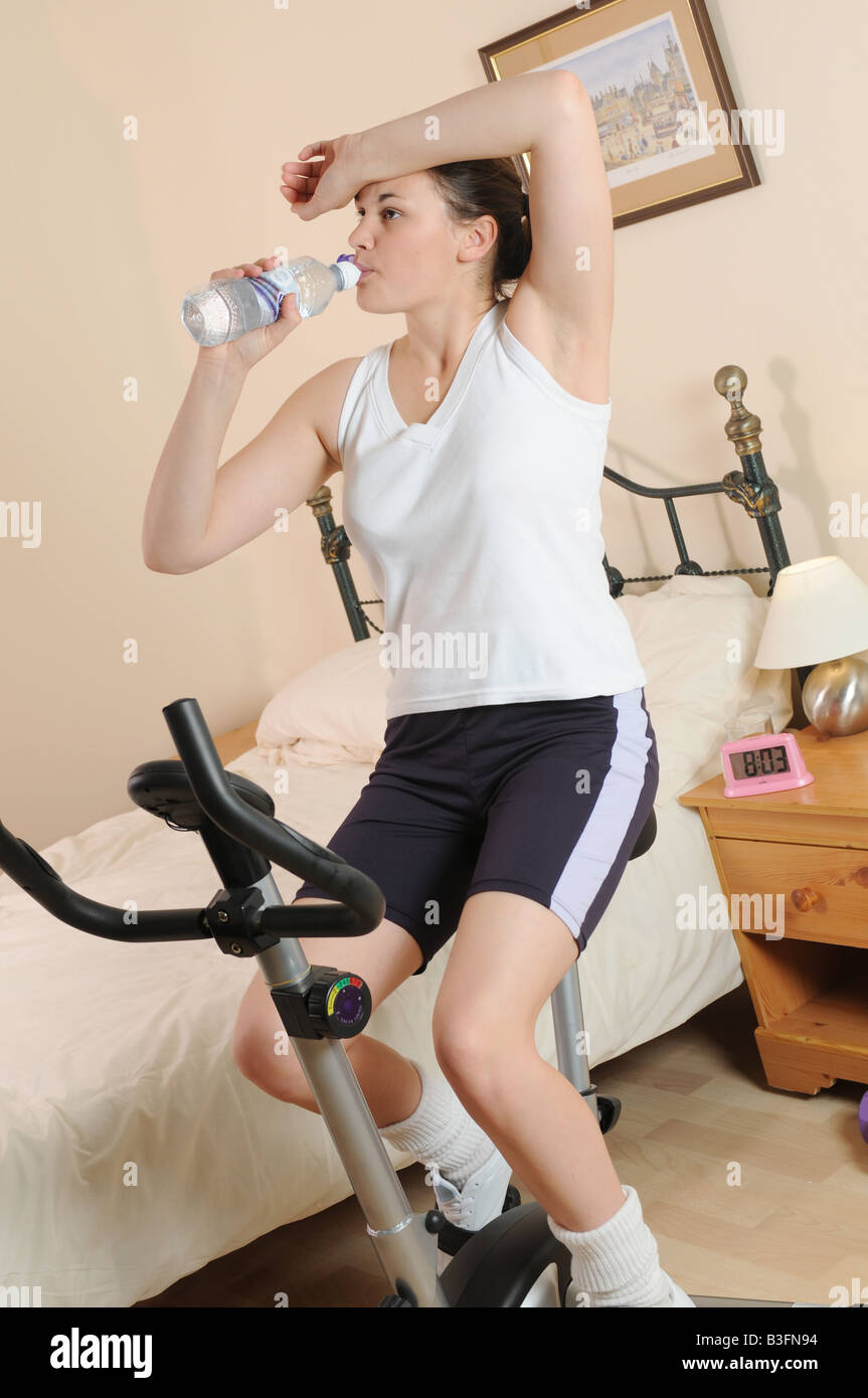 a girl fitness training on her exercise bike drinking a bottle of water ...