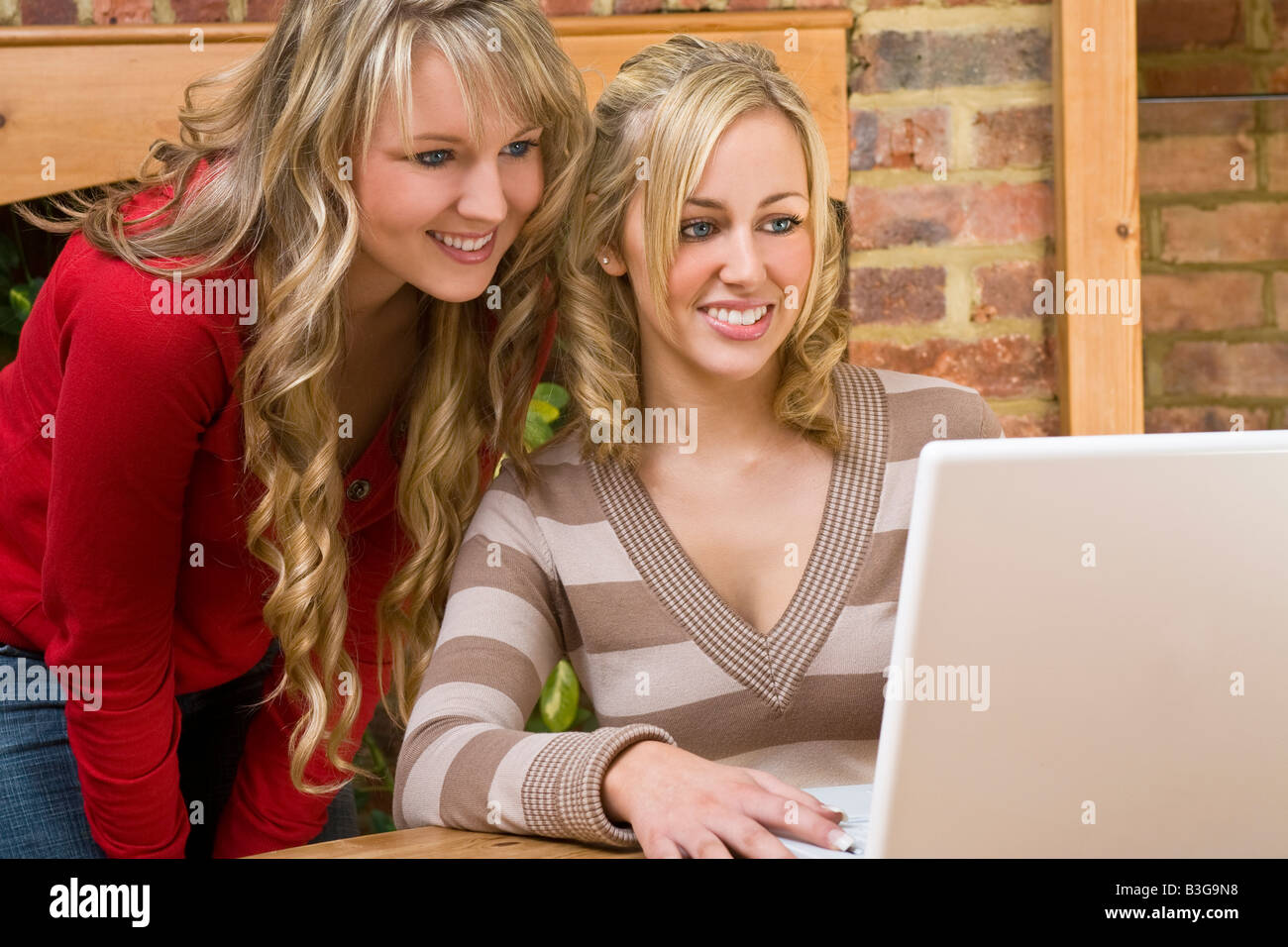 Two beautiful young women at home using a laptop computer together ...