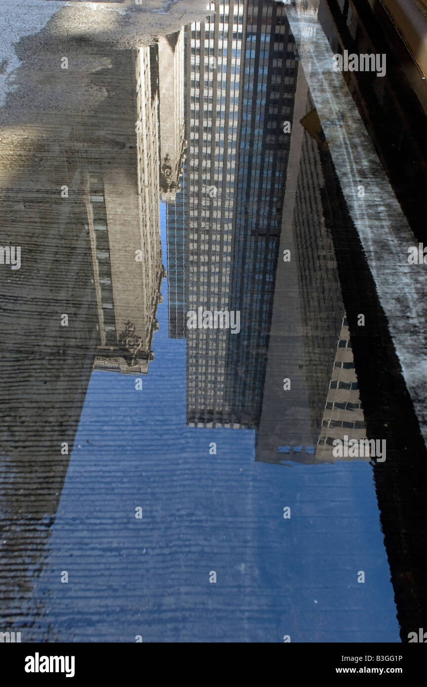 Skyscrapers reflected in a puddle of water on a street in New York ...