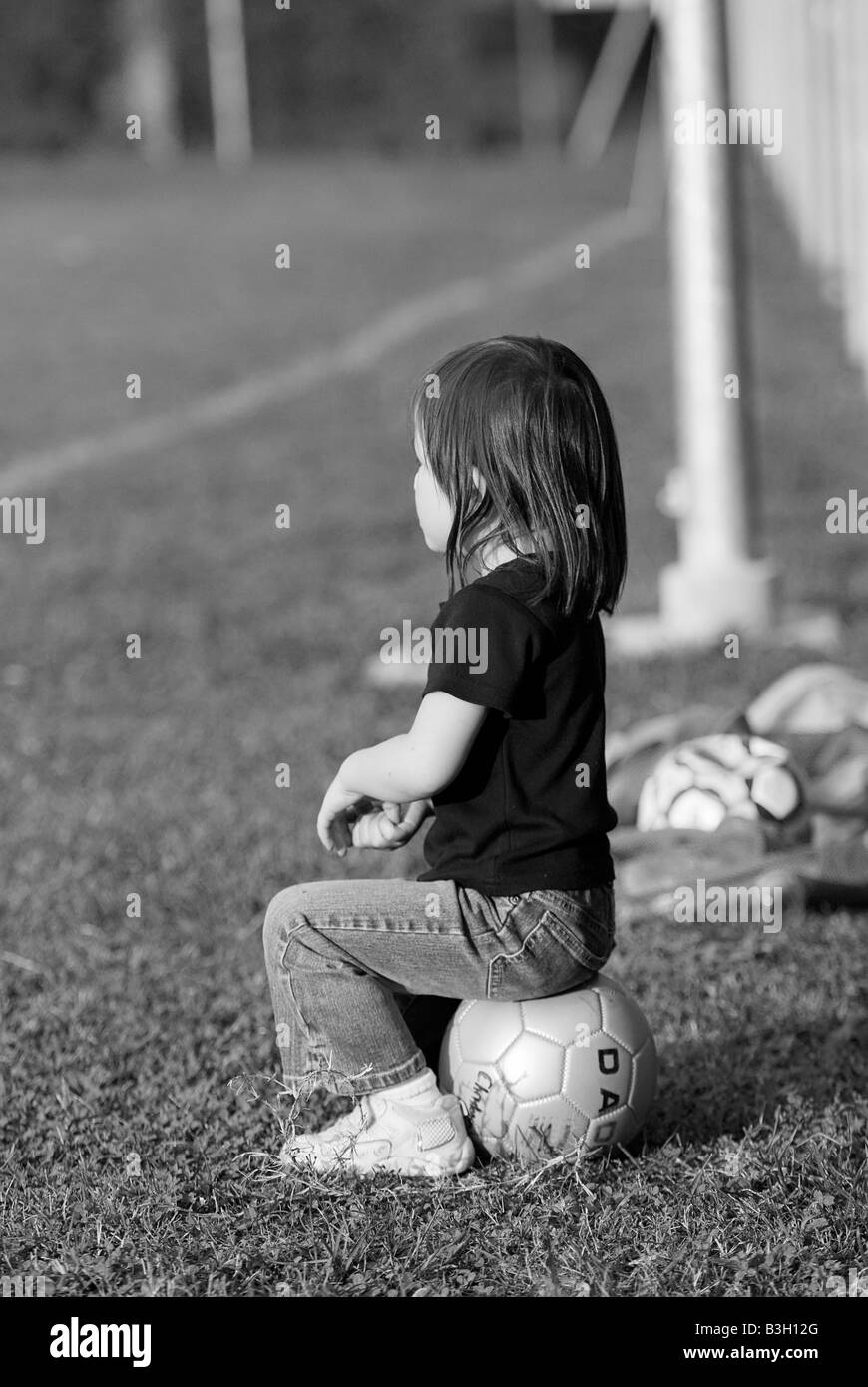 A small child sitting on a soccer ball on the sideline Stock Photo - Alamy