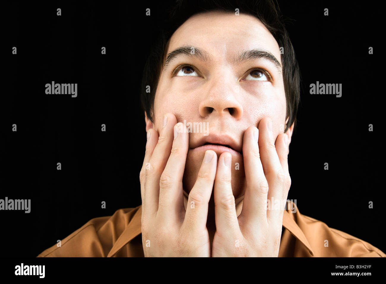 Portrait of Asian young man with hands on face looking up Stock Photo ...