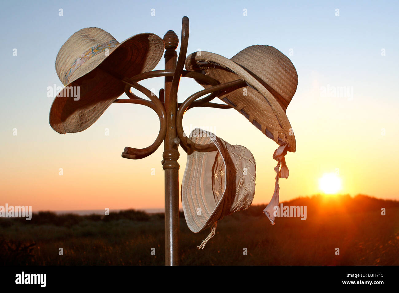 three straw holiday sun hats on a wooden hatstand against a setting sun ...