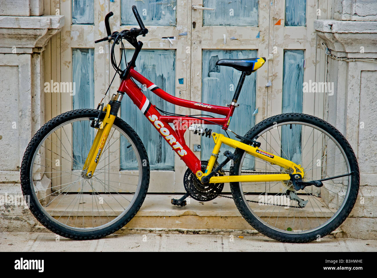 A modern, red and yellow bicycle against an ancient blue and white wall ...