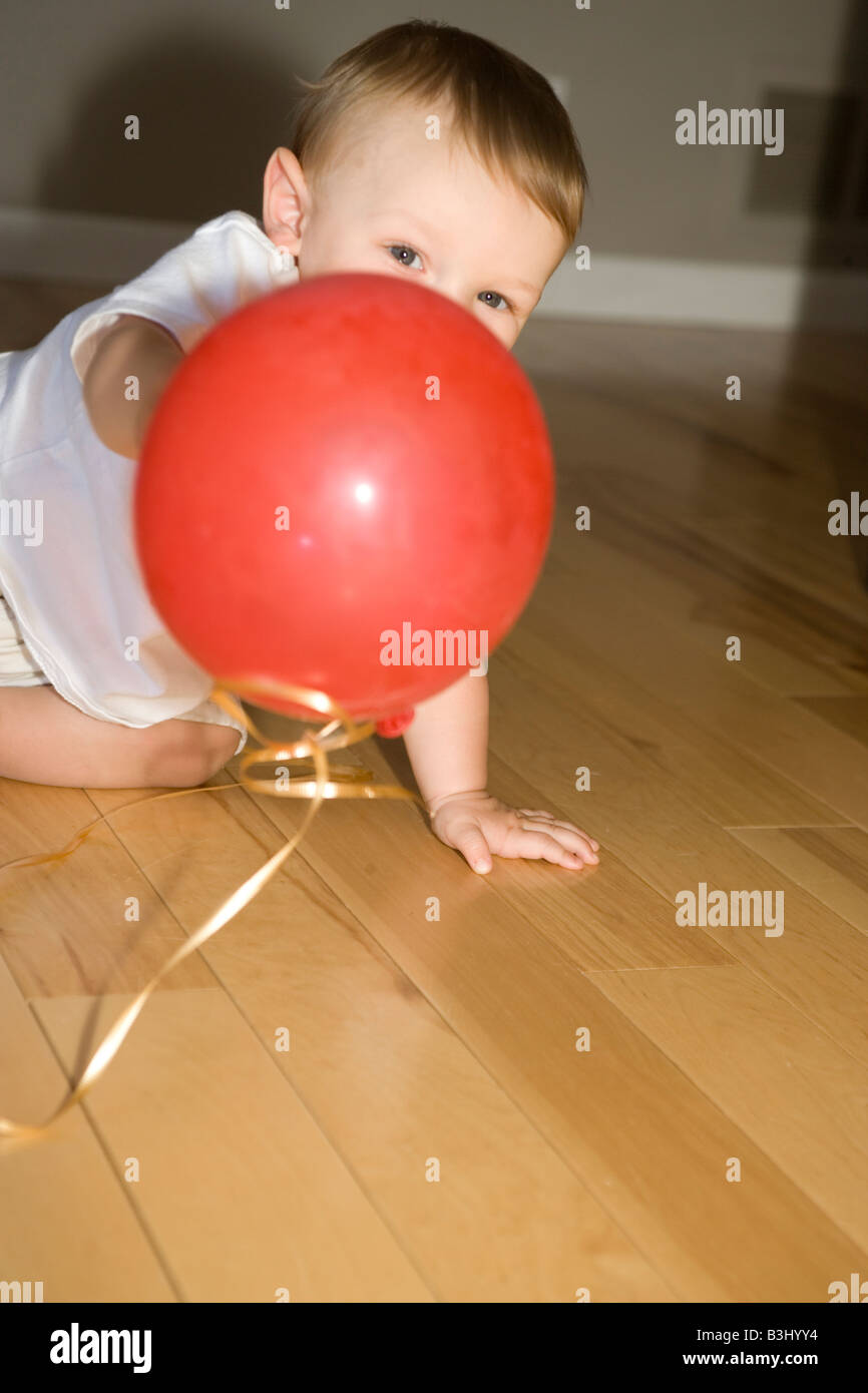 baby boy sitting up on his own and playing with a red balloon, tapping ...