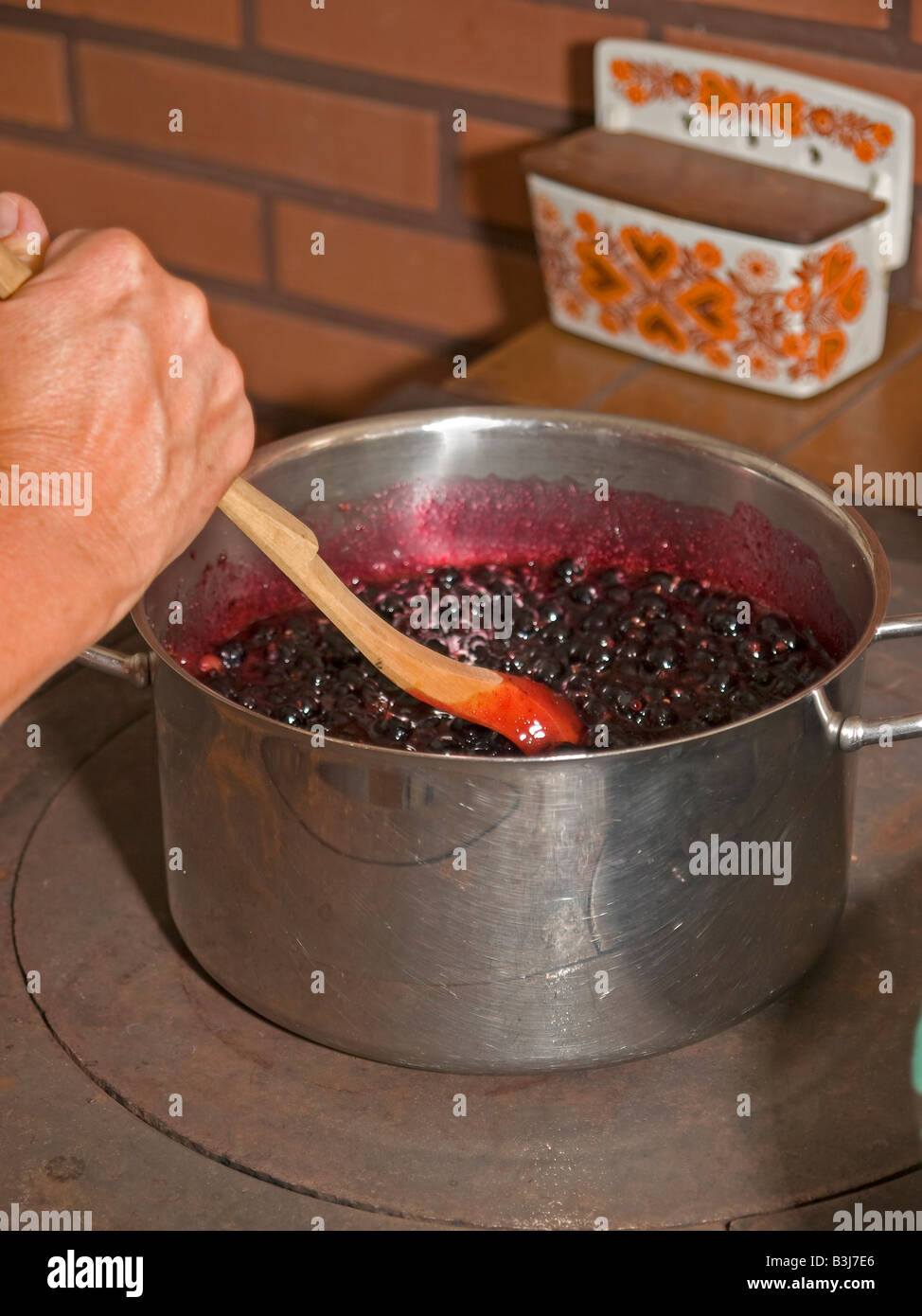 cooking jam in a steal pot stiring sugar with berries hand mixing with ...