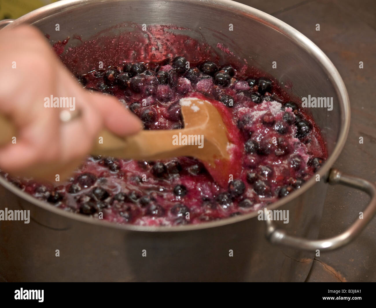 cooking jam in a steal pot stiring sugar with berries hand mixing with ...