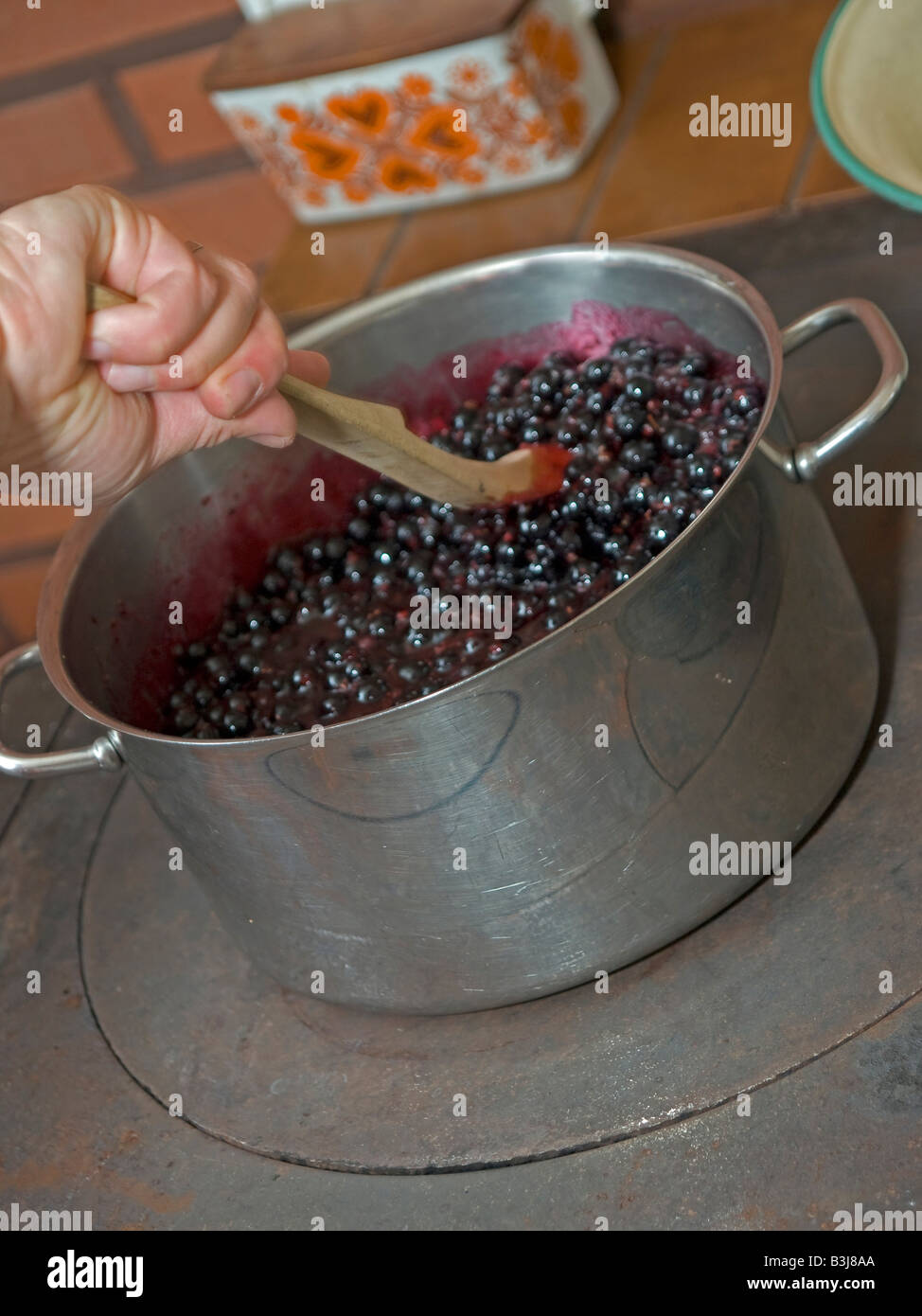 cooking jam in a steal pot stiring sugar with berries hand mixing with ...