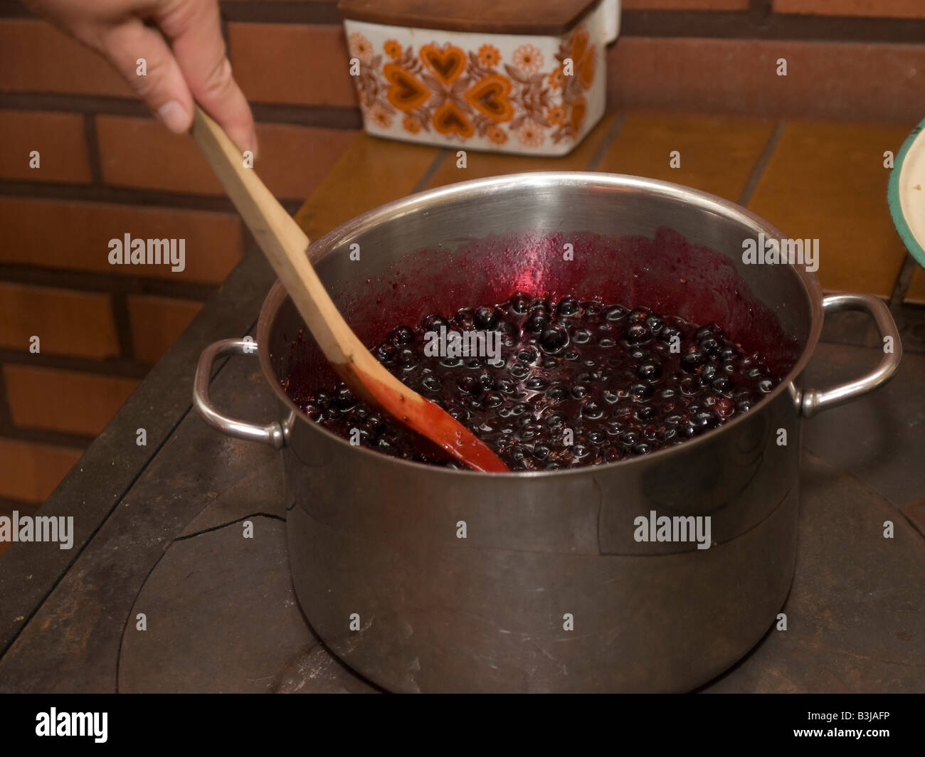 cooking jam in a steal pot stiring sugar with berries hand mixing with ...