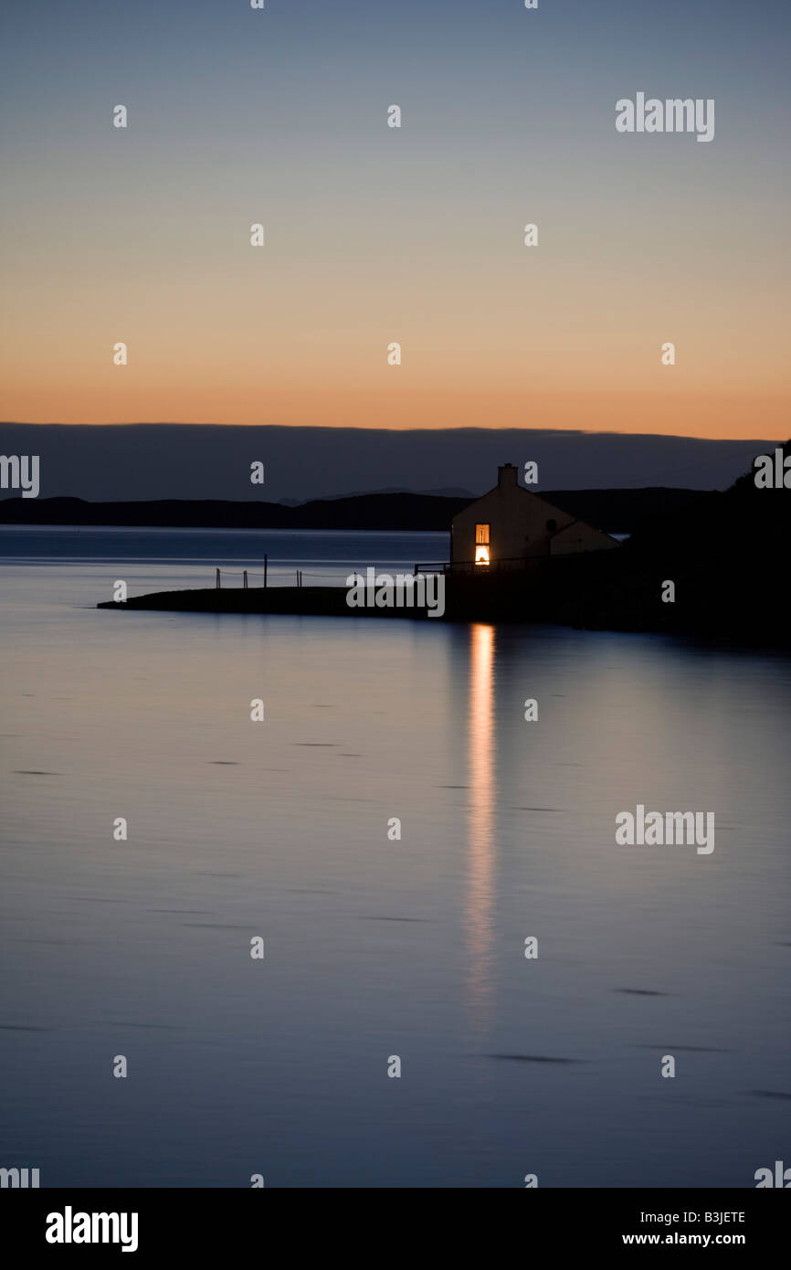 A bright window light shines across the still Loch Bay from a remote ...