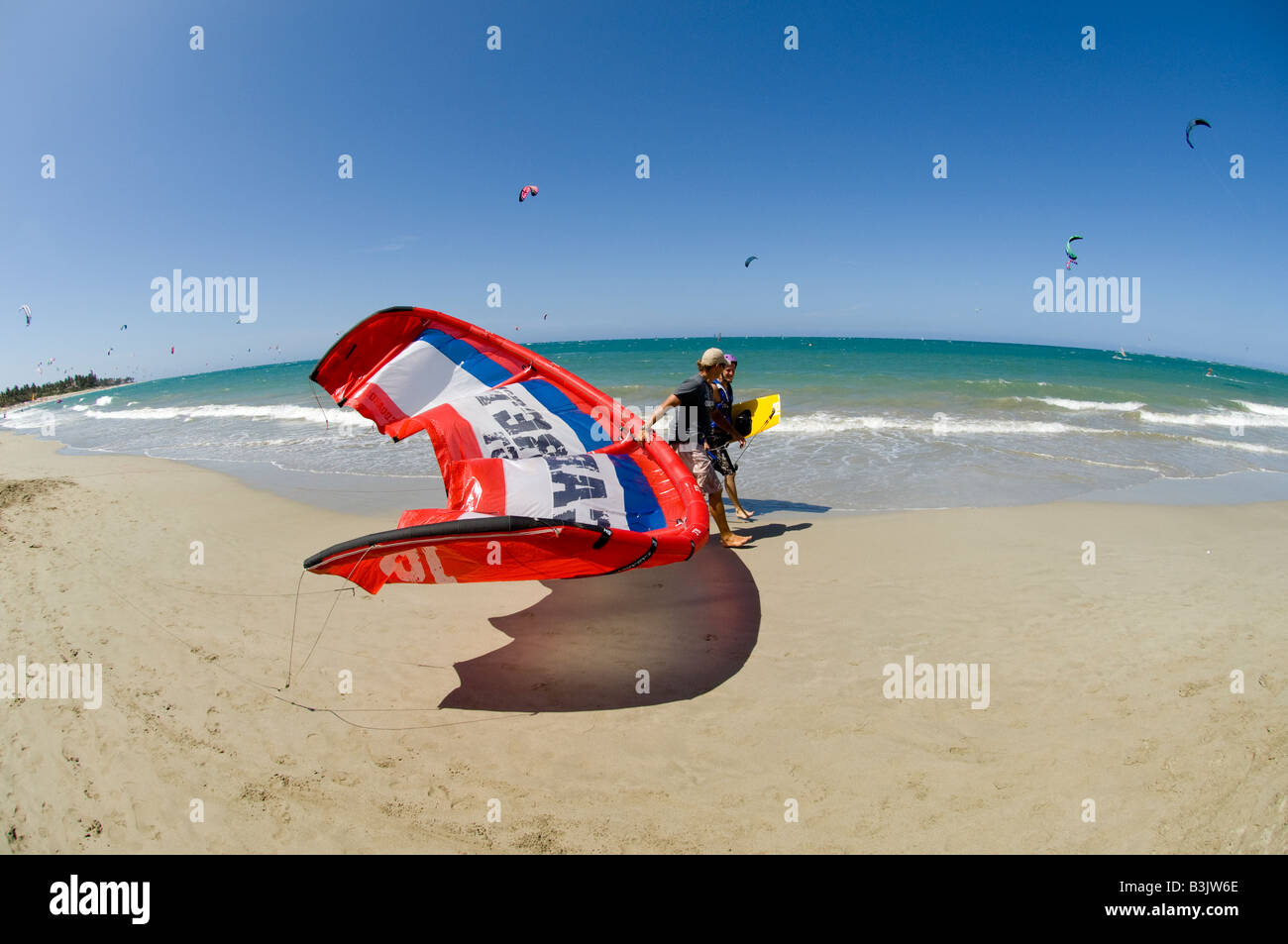 An instructor kiteboarder carries the kite for a young learner along ...