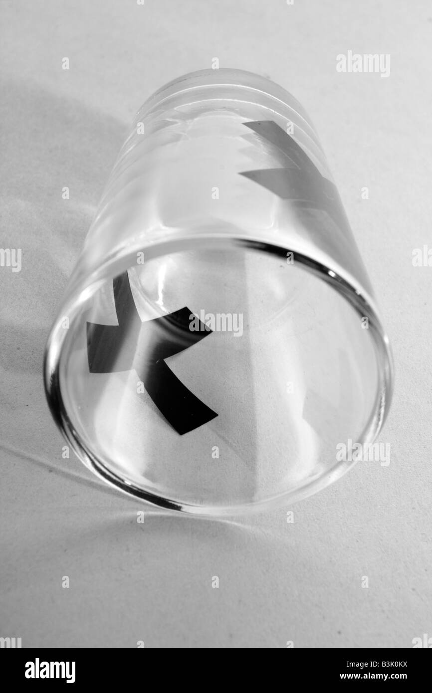 Laying on its side, a clear shotglass with two black X markings on ...