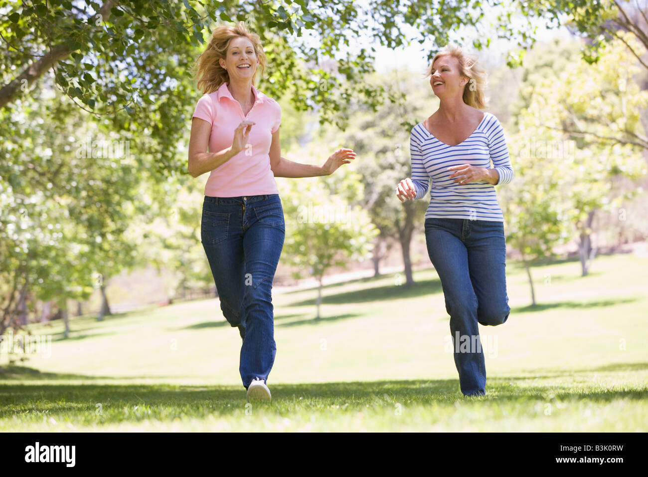 Two women running in park and smiling Stock Photo - Alamy