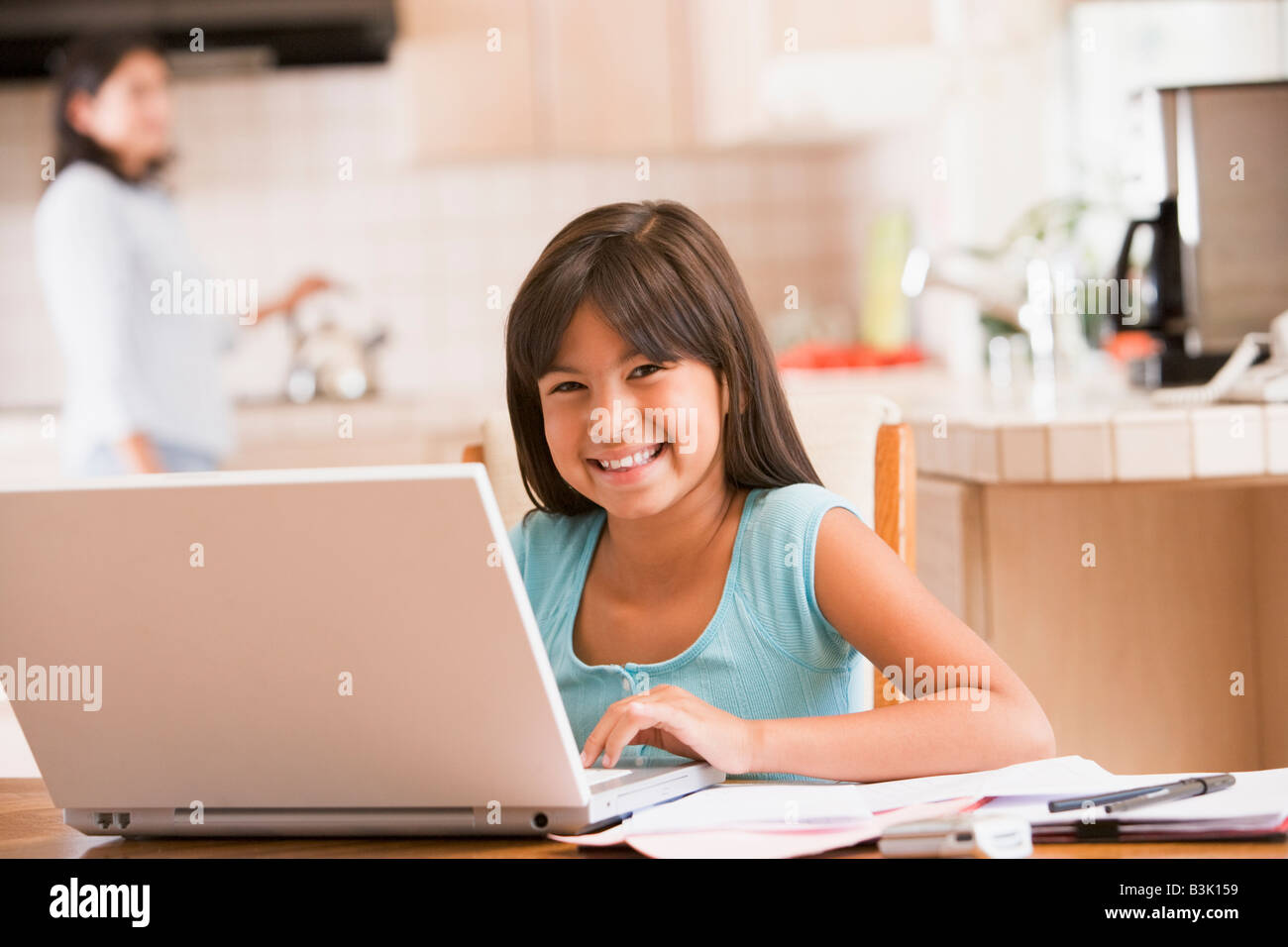 Young girl in kitchen with laptop and paperwork smiling with woman in ...