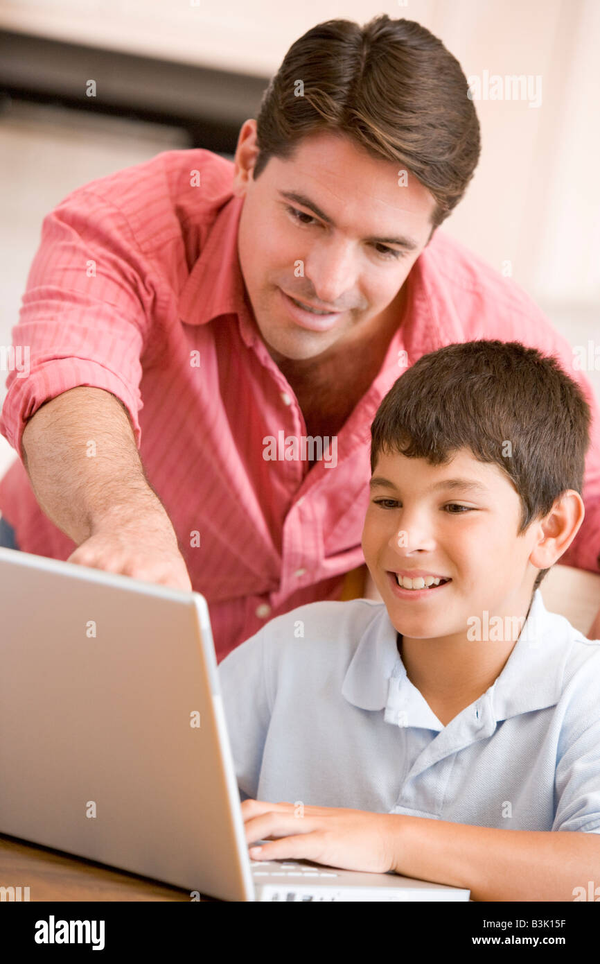 Man helping young boy in kitchen with laptop smiling Stock Photo - Alamy
