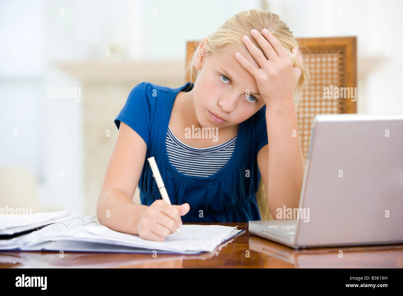 Young girl with laptop doing homework in dining room looking unhappy ...