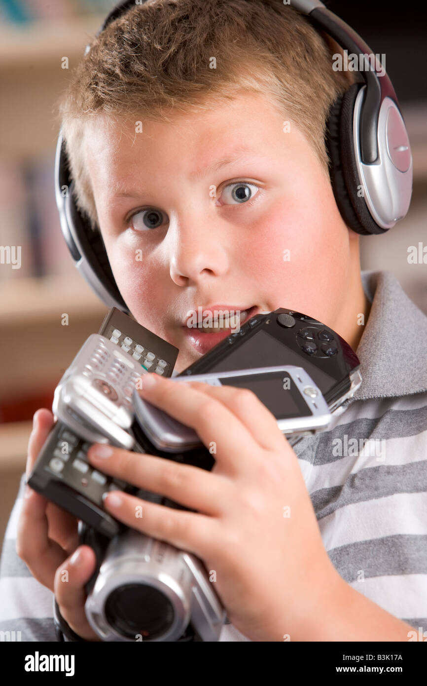 Young boy wearing headphones in bedroom holding many electronic devices ...