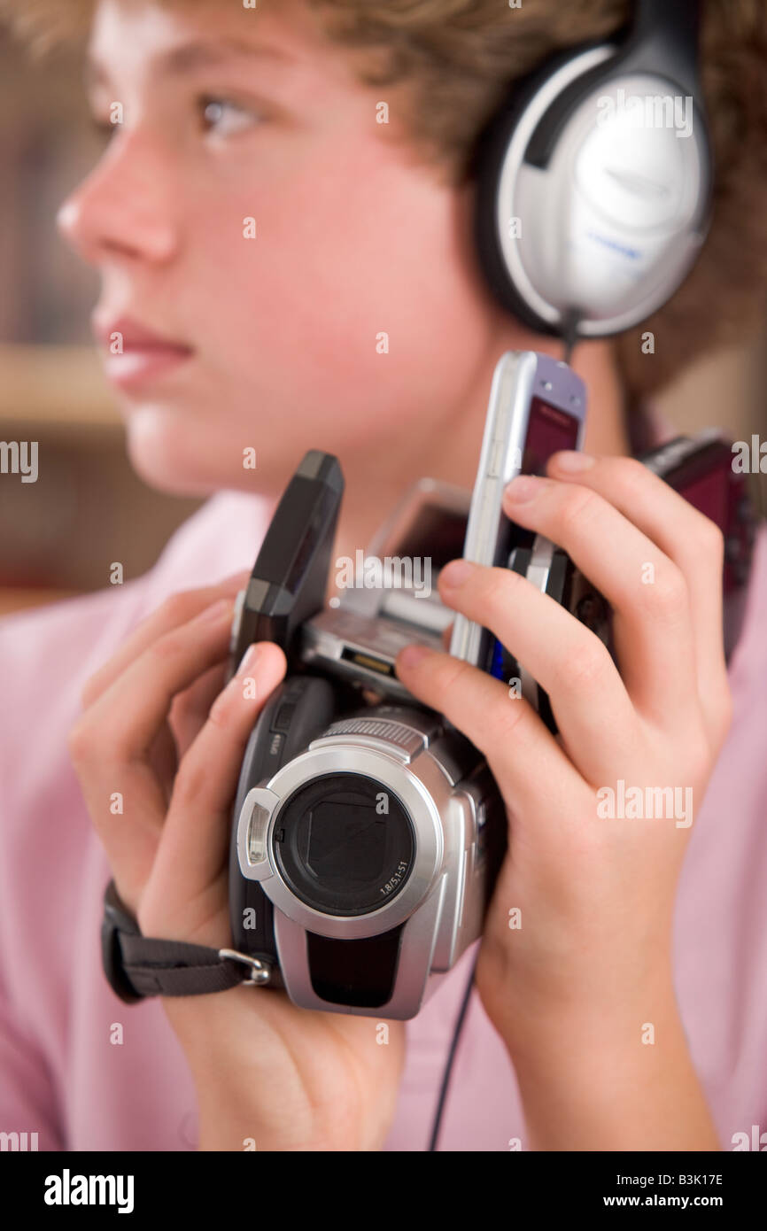 Young boy wearing headphones in bedroom holding many electronic devices ...