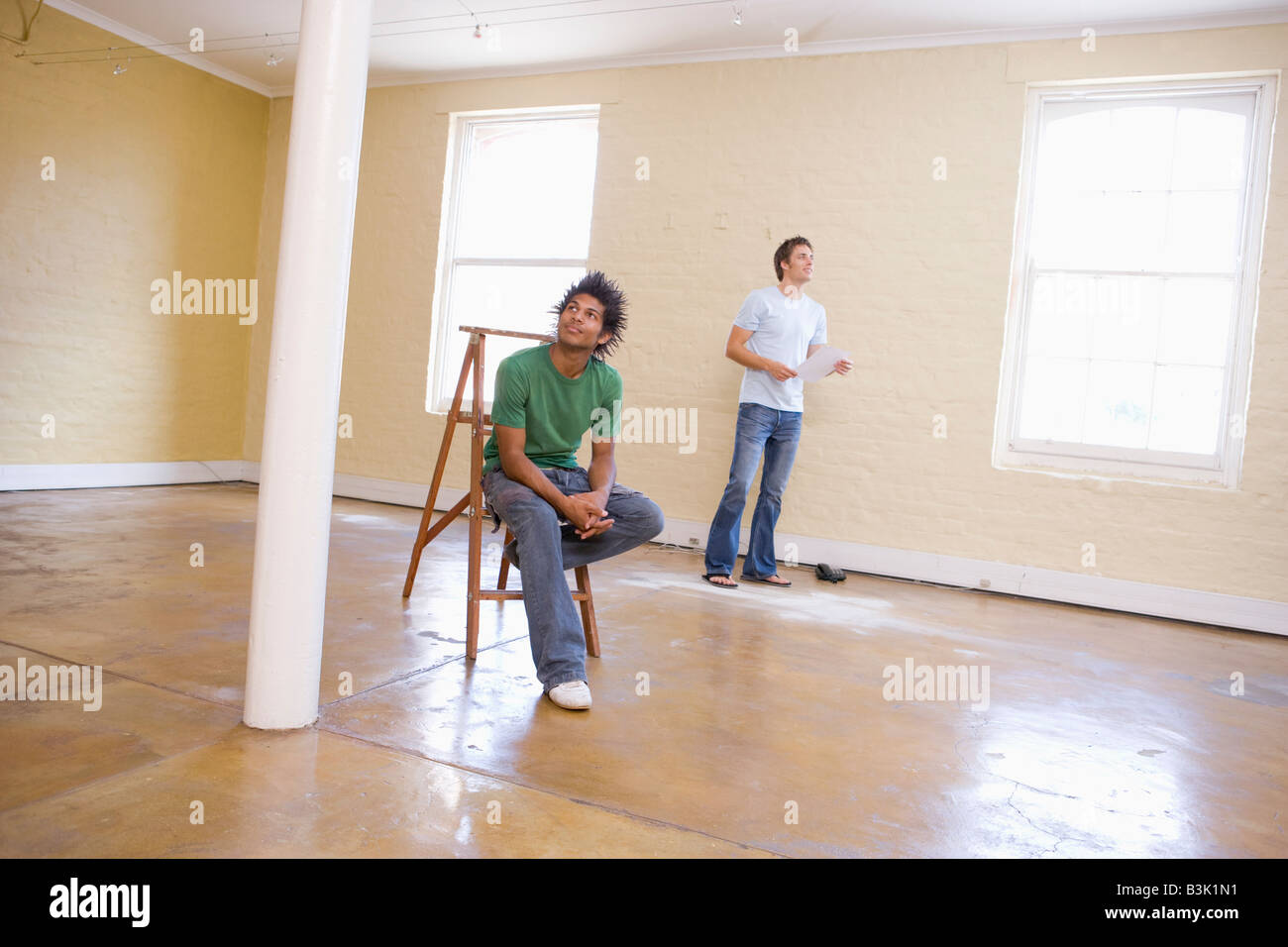 Two men in empty space with ladder holding paper Stock Photo - Alamy