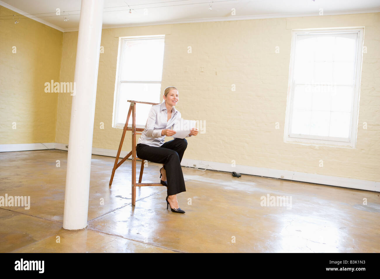 Woman sitting on ladder in empty space holding paper smiling Stock ...